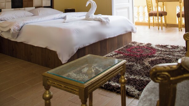 Quarto de hotel com cama grande, uma mesinha, varanda com vista e janela com cortinas.