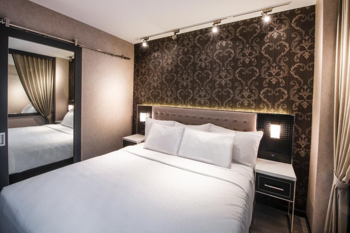 Quarto de hotel com uma cama grande, um espelho, uma mesa de cabeceira e uma parede com design estampado.