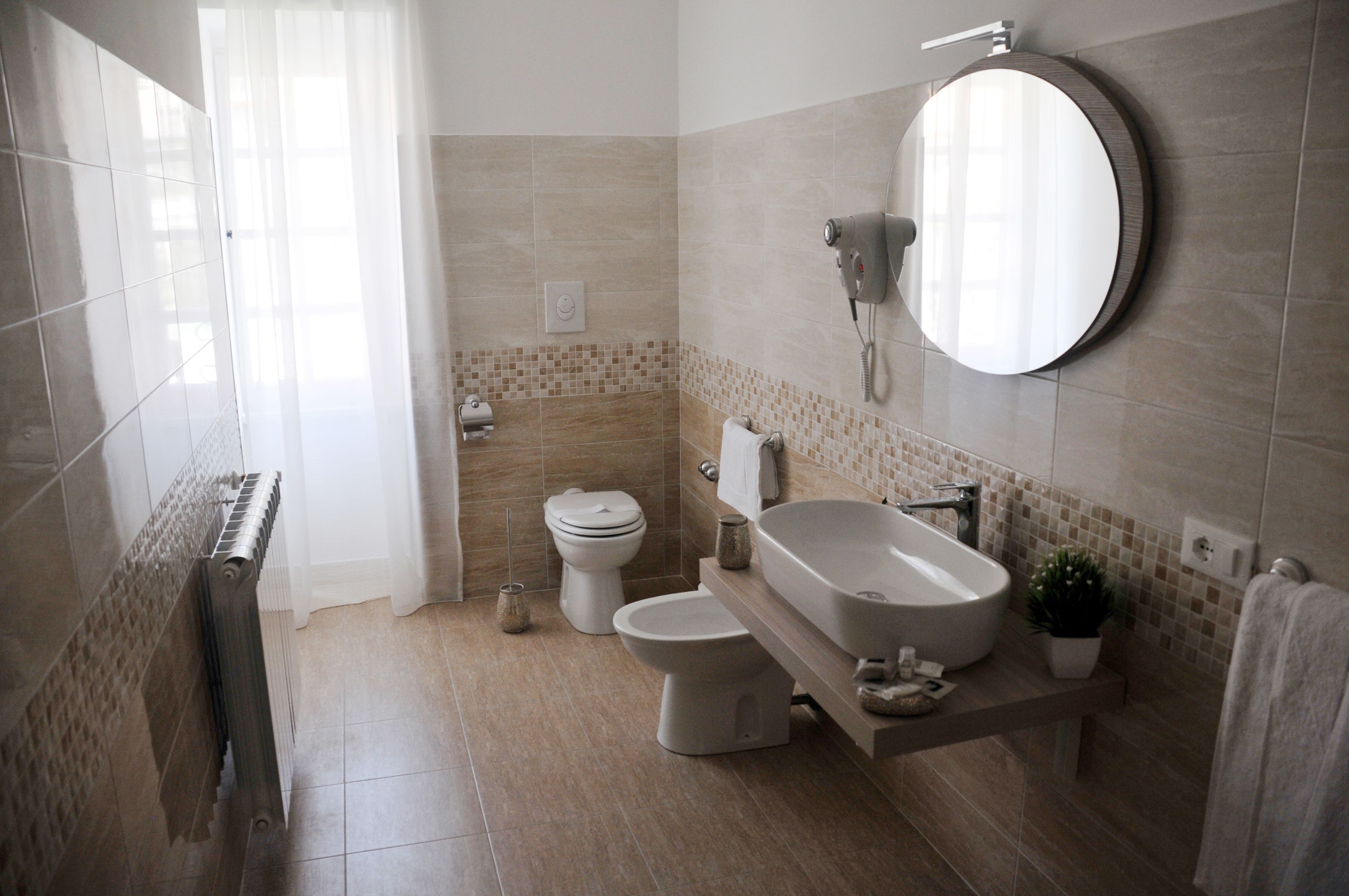 Uma casa de banho moderna com banheira, sanita e bidé. Possui um espelho grande, um porta-toalhas e uma planta em vaso.