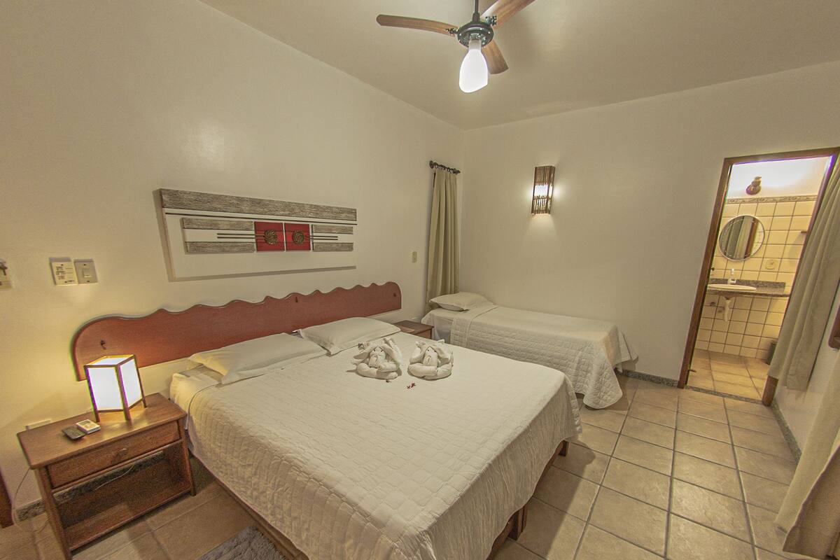 Quarto de hotel com cama, mesa de cabeceira e ventoinha no teto.