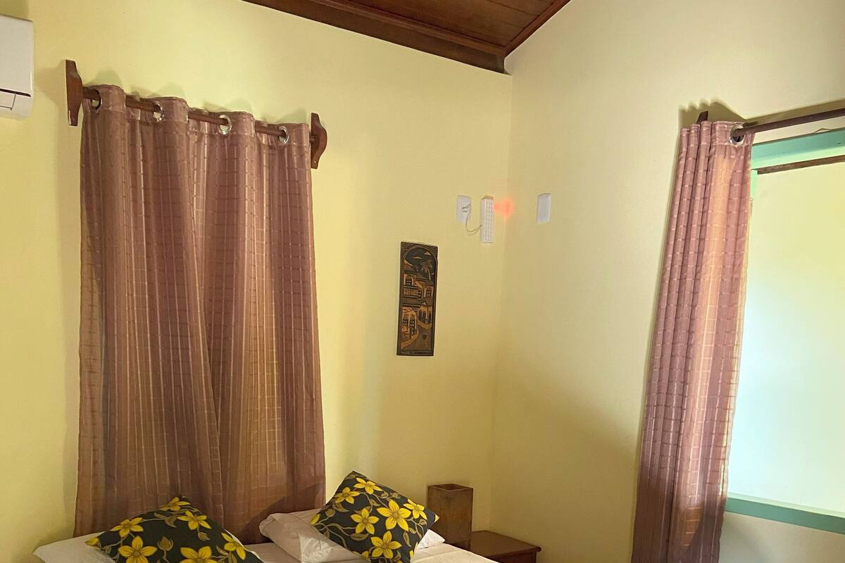 Uma cama de casal com cabeceira marrom, duas almofadas com estampas florais amarelas e um cobertor marrom.