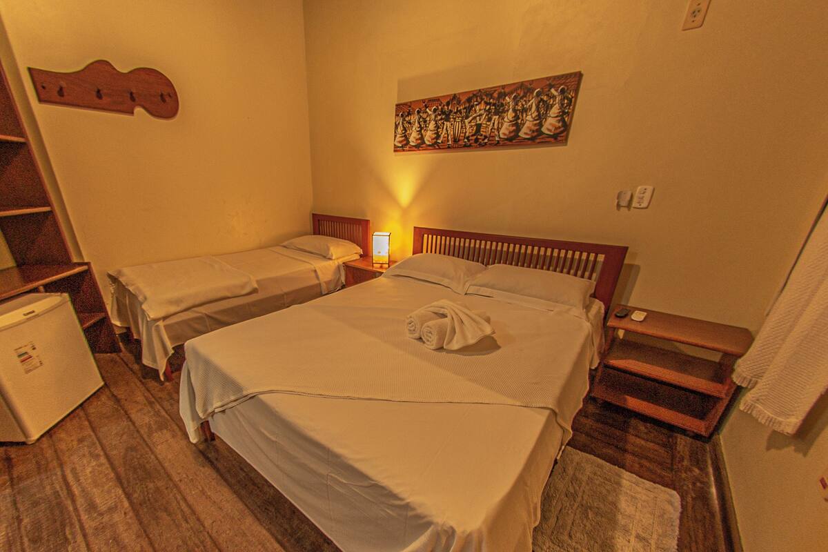 Quarto de hotel com duas camas, um pequeno frigorífico, uma guitarra e um quadro na parede.