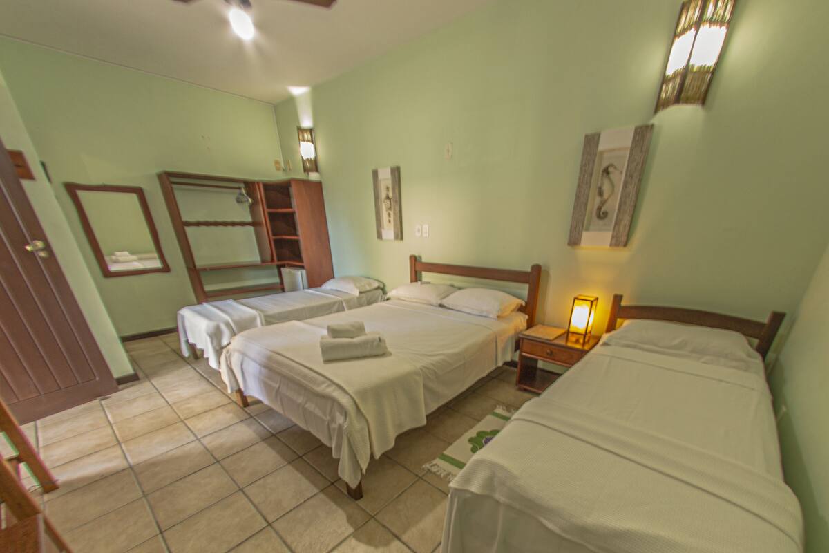 Quarto com duas camas de solteiro, um guarda-roupa de madeira, um espelho e uma pequena mesa com abajur.