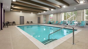 Uma piscina interior com água cristalina, rodeada por espreguiçadeiras e mesas.