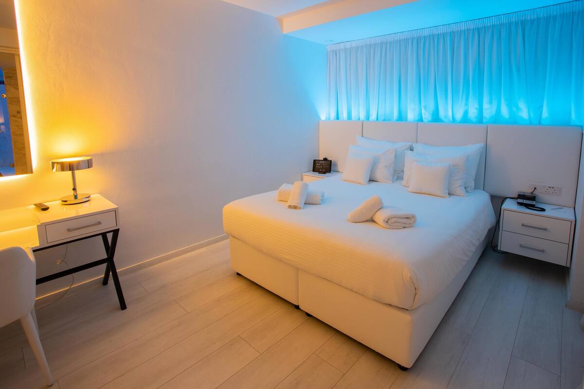 Quarto moderno com cama grande, mesas de cabeceira, escrivaninha e uma cadeira.