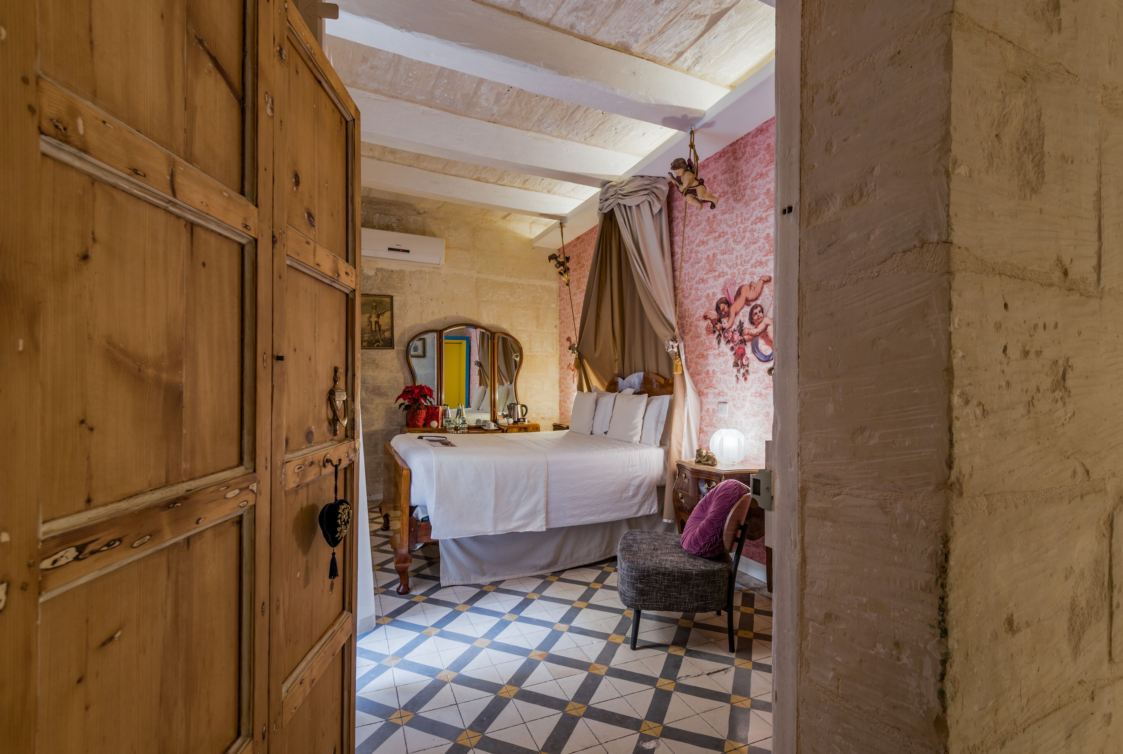 Um quarto com piso xadrez, cama com dossel, guarda-roupa de madeira e espelho na parede.