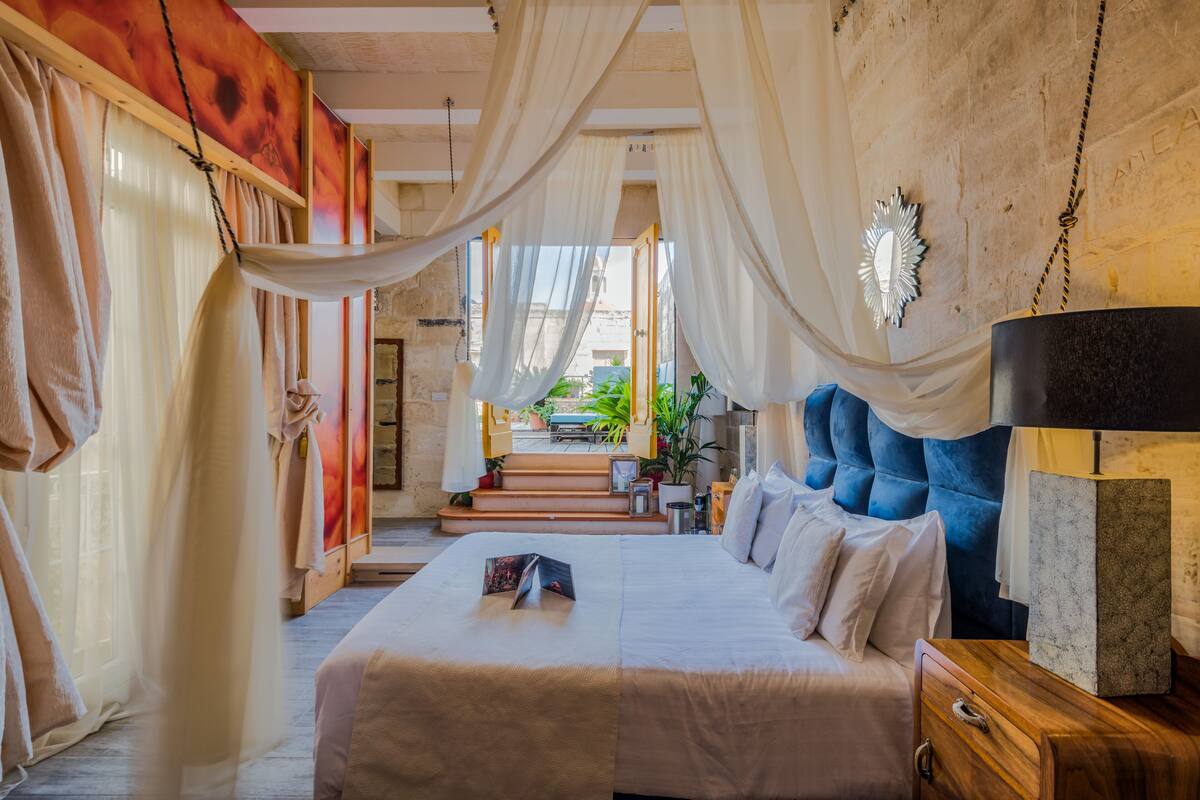 Quarto com uma cama grande, uma mesa de cabeceira de madeira e vista para o exterior.