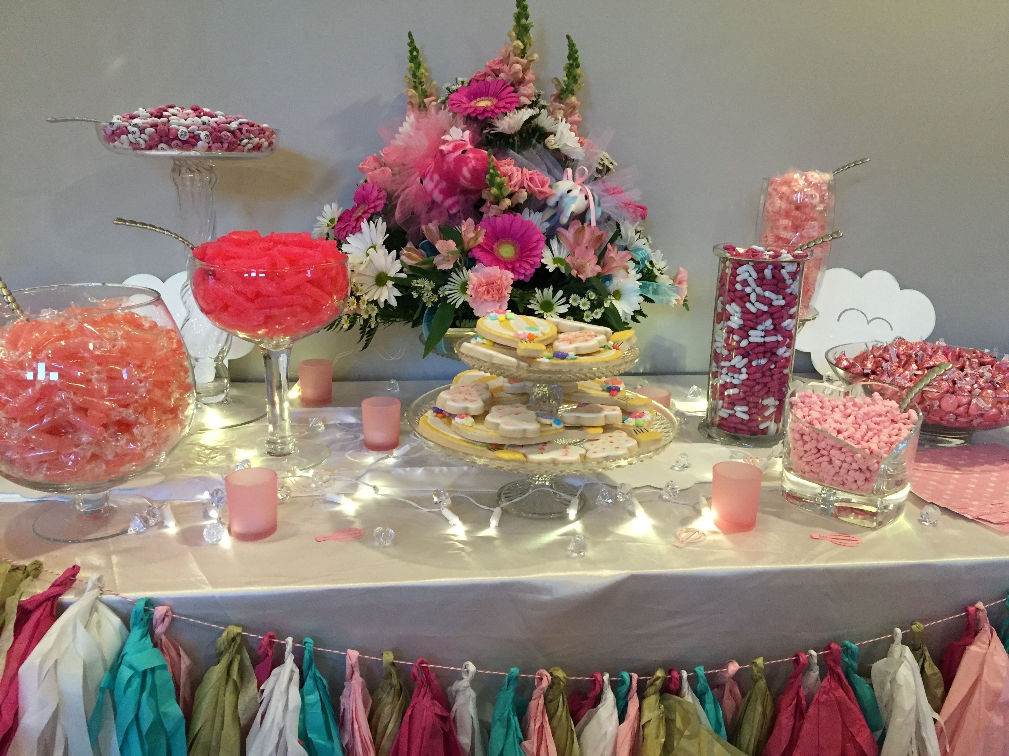 Mesa com diversos alimentos e decorações, incluindo um arranjo floral e guardanapos coloridos.