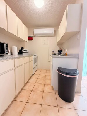 Cozinha compacta com armários brancos, micro-ondas, fogão e lixeira.