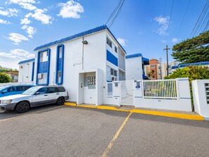 Um edifício com portão fechado, esquema de cores branco e azul, e um carro branco estacionado em frente.