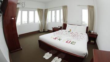 Quarto de hotel com uma cama grande, duas mesas de cabeceira, um guarda-roupa e duas janelas com cortinas.