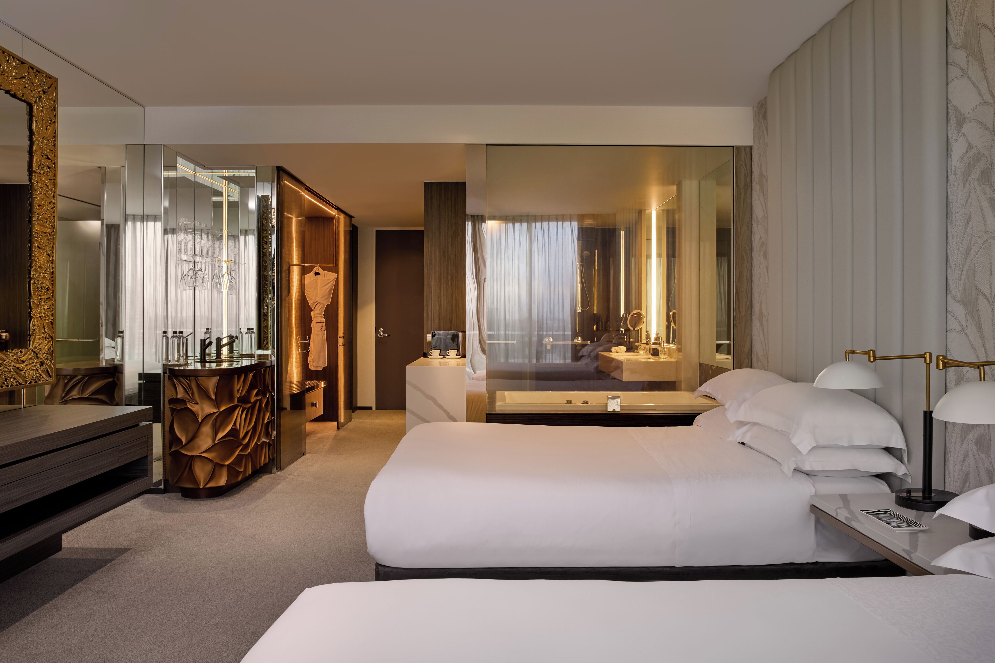 Quarto de hotel moderno com uma cama grande, uma toucador com espelho e um espaço de estar com mesa e cadeiras.