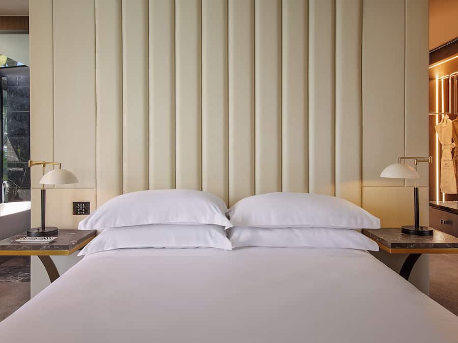 Quarto de hotel com uma cama grande, duas mesas de cabeceira com luminárias, uma penteadeira com espelho e vista para uma varanda.