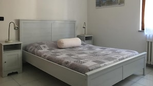 Quarto com cama, mesas de cabeceira e janela.
