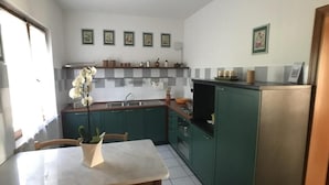 Uma cozinha compacta com armários verdes, painel de azulejos e área de refeições com mesa e cadeiras.