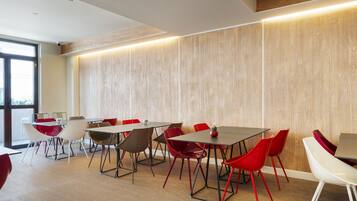 Uma sala de conferências moderna com várias mesas e cadeiras, janelas amplas e um painel de madeira decorativo.