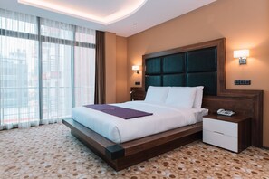 Quarto de hotel com uma cama grande, mesa de cabeceira e janela com cortinas.