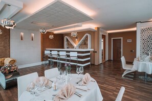 Uma sala de jantar moderna com um bar central, cadeiras brancas e piso de madeira.