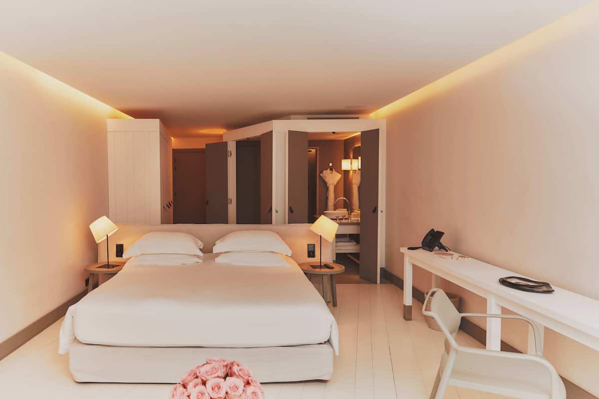 Quarto de hotel moderno com uma cama grande, mesas de cabeceira, uma escrivaninha e uma cadeira.