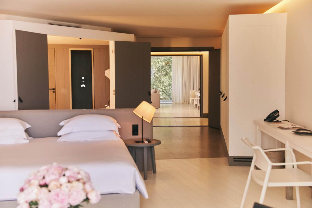 Quarto de hotel moderno com cama grande, mesa de cabeceira, abajur e escrivaninha com cadeira.