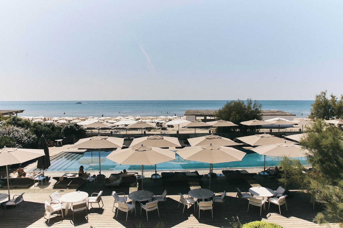 Área de piscina com vários guarda-sóis e espreguiçadeiras, com vista para um mar azul e límpido.