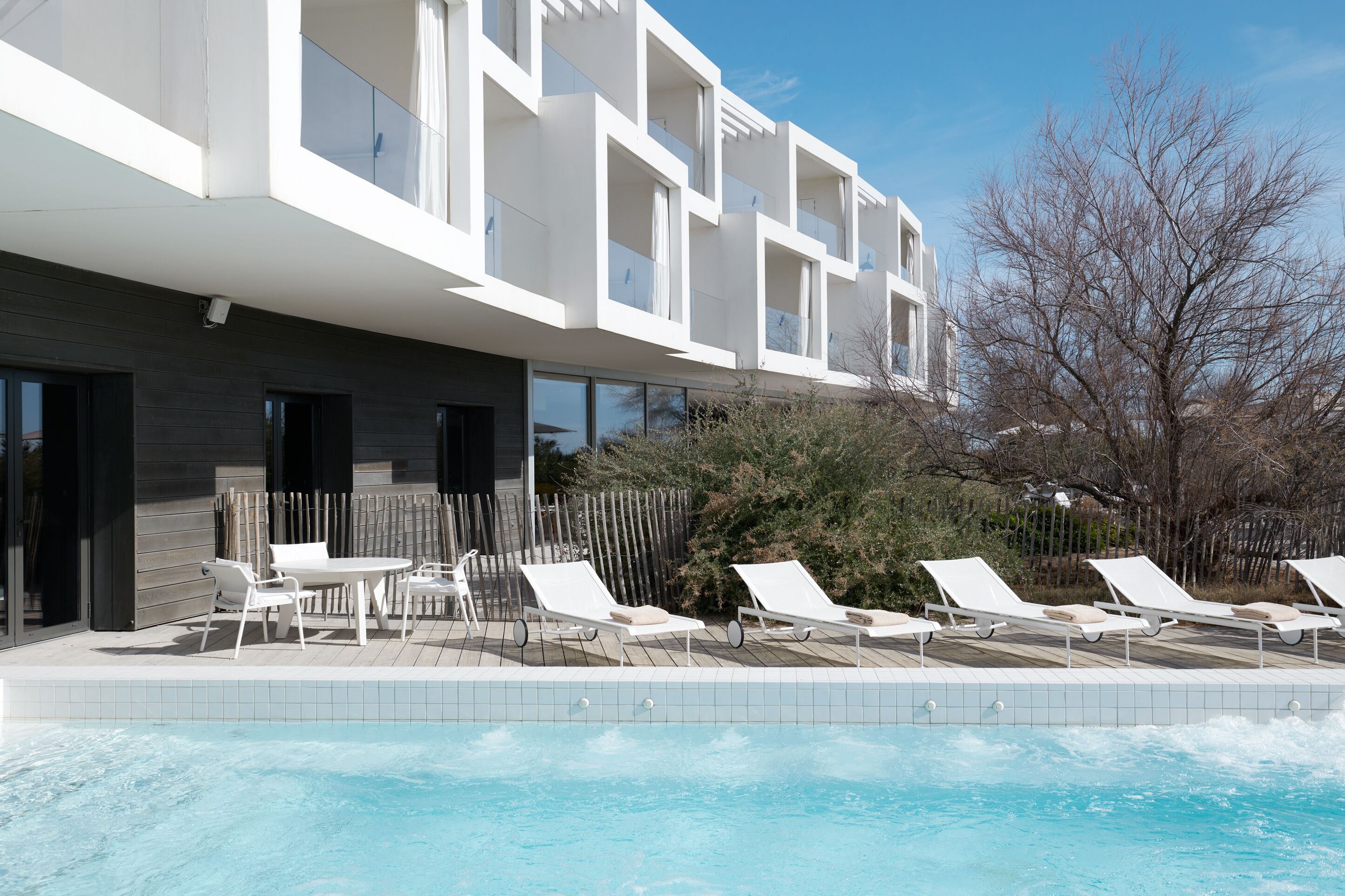 Um edifício moderno com área de piscina, incluindo espreguiçadeiras e uma mesa.