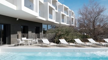 Um edifício moderno com área de piscina, incluindo espreguiçadeiras e uma mesa.