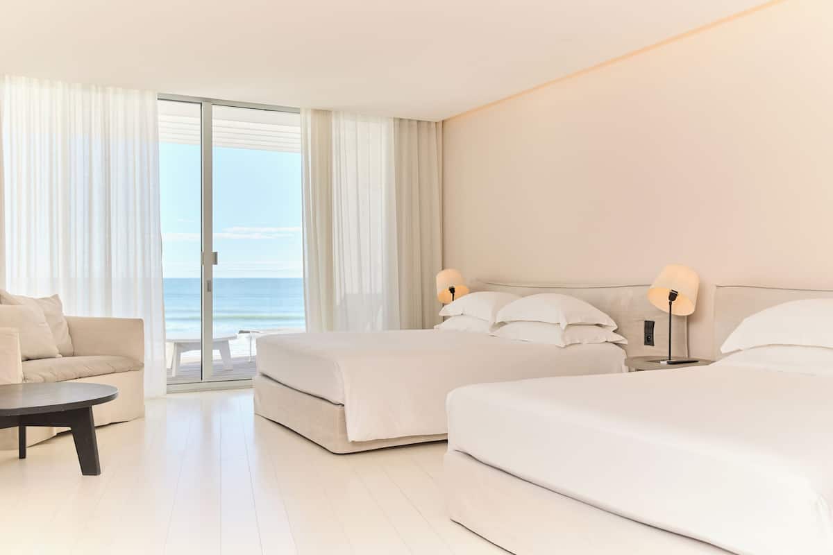 Quarto de hotel com cama, sofá, mesa e vista para o oceano.