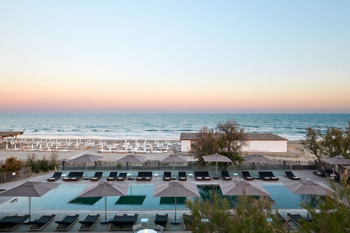 Um resort com área de piscina, espreguiçadeiras e vista para o oceano ao pôr do sol.