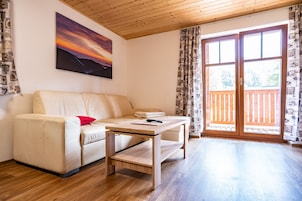 Uma sala de estar com sofá, mesa de centro e uma janela grande com cortinas.