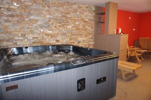 Uma área de spa moderna com parede de pedra, banheira de hidromassagem e mobiliário de madeira.