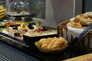 Buffet com diversos alimentos, incluindo pão, frutas e carnes.