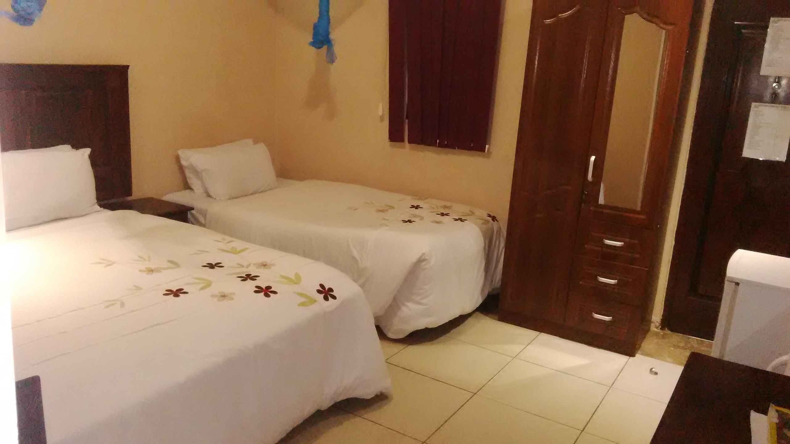 Quarto pequeno e limpo, com duas camas, um guarda-roupa de madeira e um banheiro.