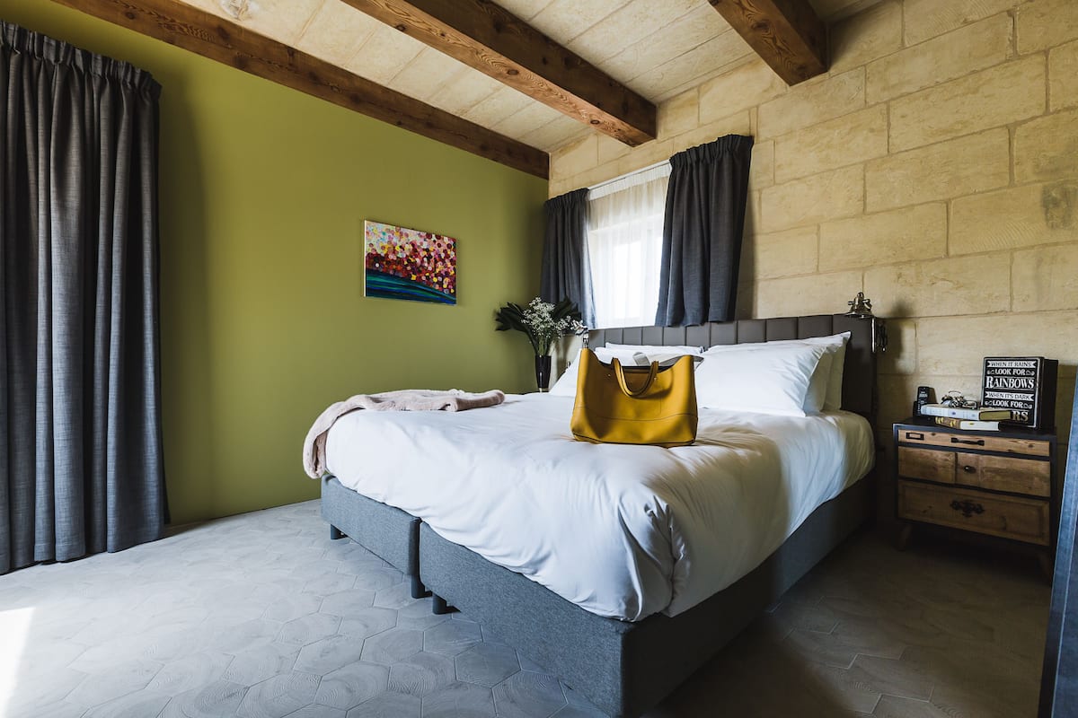 Quarto com cama, mesa de cabeceira, janela com cortinas e um quadro na parede.