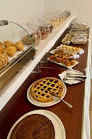 Um buffet com diversos produtos de pastelaria e sobremesas, incluindo doces, tortas e um bolo.