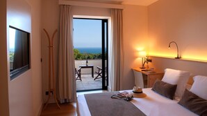 Quarto de hotel com cama, escrivaninha, cadeira, mesa, televisão e varanda vista para o mar.