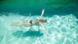 Pessoa nadando em piscina transparente com escada visível e um dreno circular.