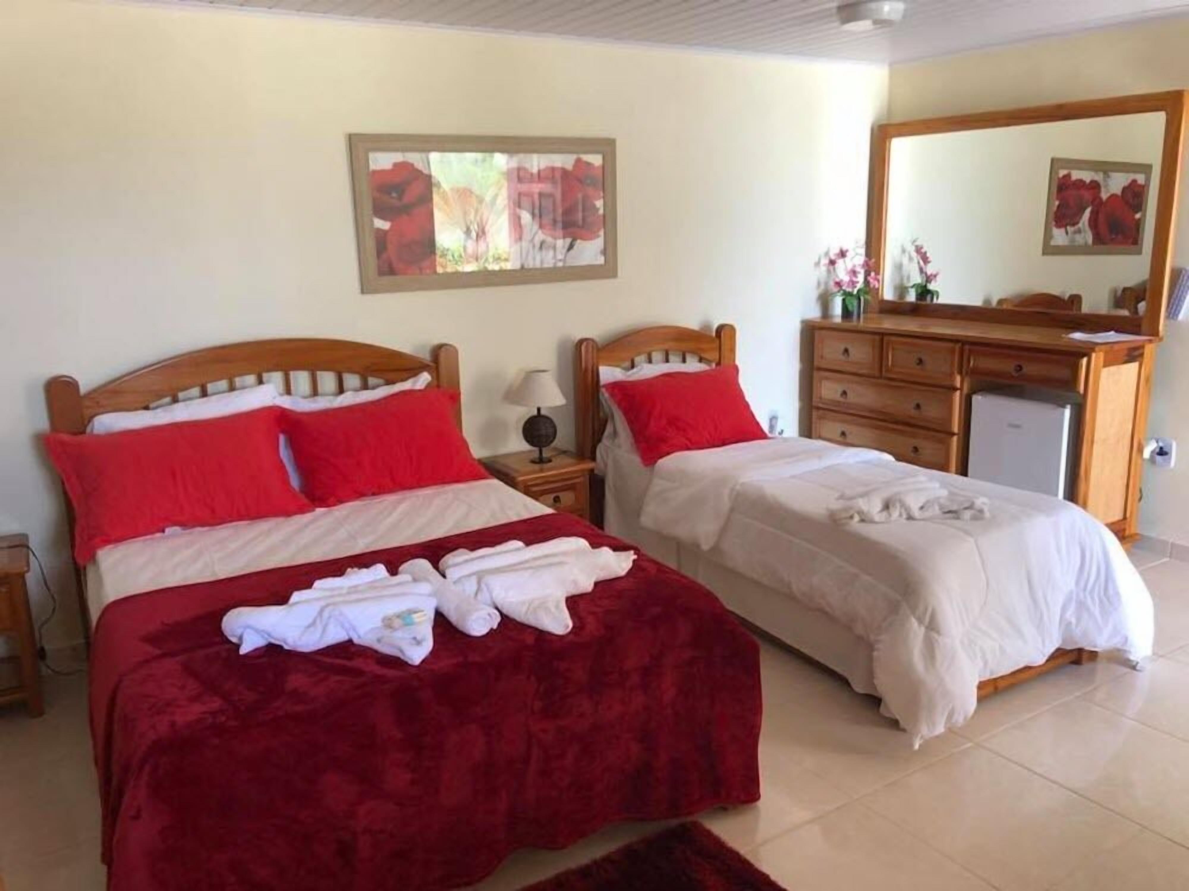 Quarto de hotel com duas camas, roupa de cama vermelha e branca, penteadeira de madeira e um espelho.