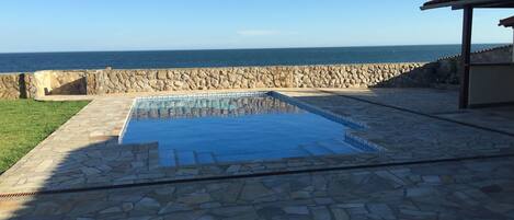Uma piscina com um pátio de pedra e vista para o oceano.