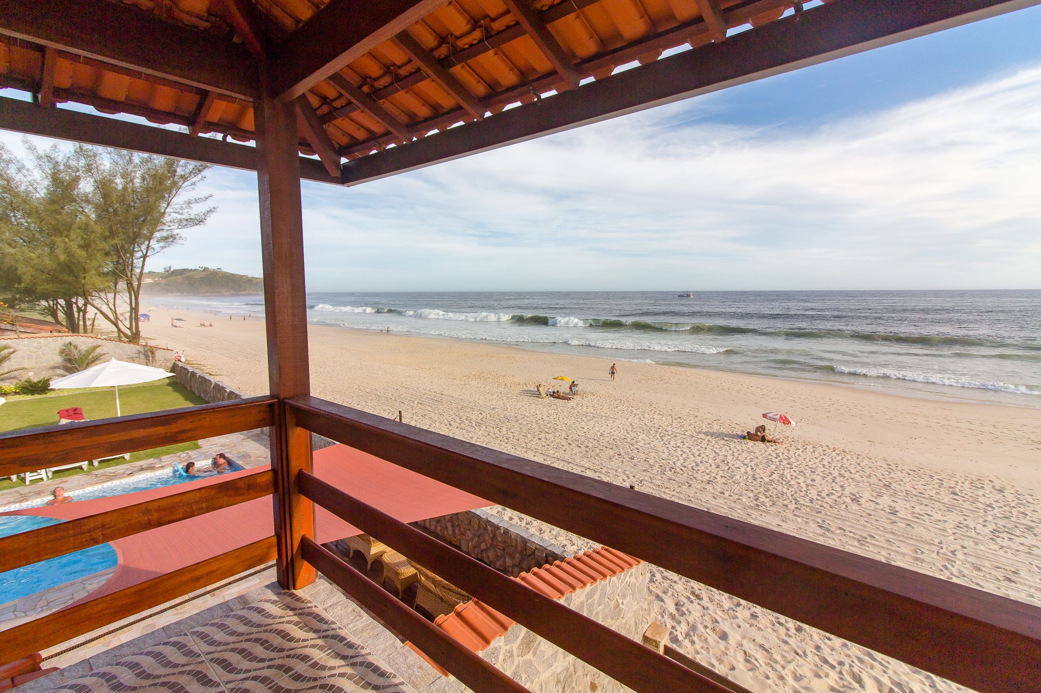 Vista da praia a partir de um espaço coberto, com piscina e guarda-sóis.