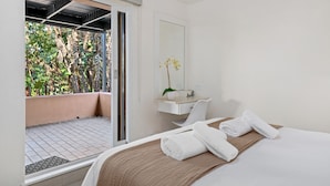 Quarto de hotel moderno com cama, banheiro com espelho e varanda com vista para área verde.