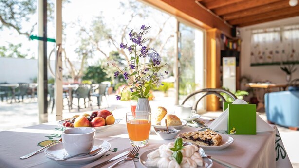 Uma mesa de café da manhã com frutas, doces e um vaso de flores.