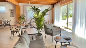Um espaço interno amplo com teto de madeira, um sofá, cadeiras, uma mesa e um vaso de planta.