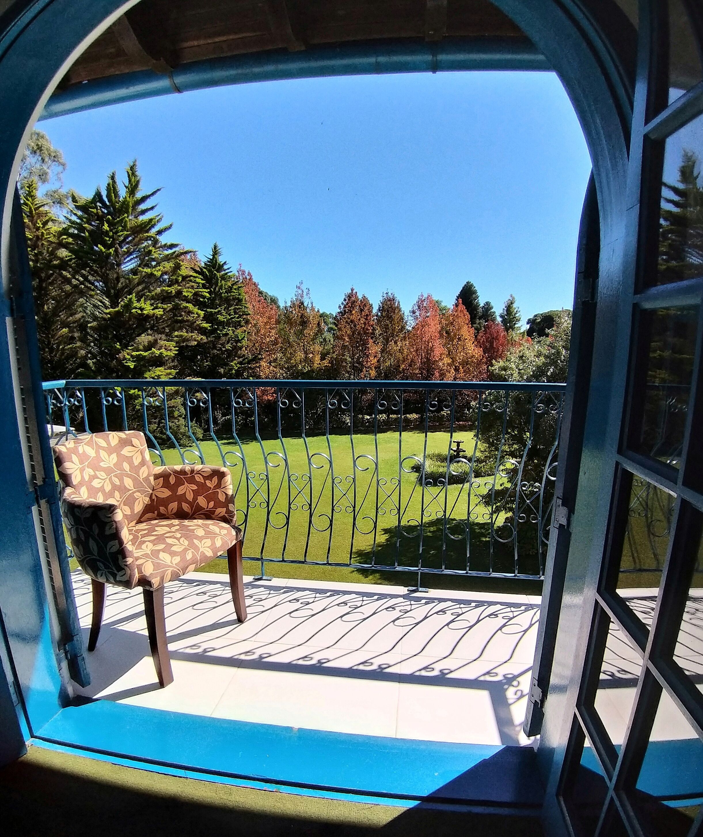 Vista de uma varanda com cadeira, guarda-corpo de metal e gramado verde com árvores.
