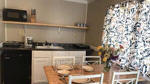 Cozinha compacta equipada com micro-ondas, máquina de café e lava-louças. Mesa de jantar posta com pratos e talheres.