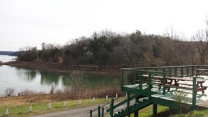 Um parque à beira do lago, com mesas de piquenique e uma escadaria verde que leva a uma plataforma de observação.