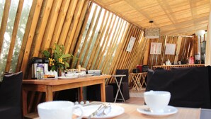 Interior em madeira com área de refeições, mesas postas com pratos e copos brancos, e um bar com liquidificador e outros eletrodomésticos.