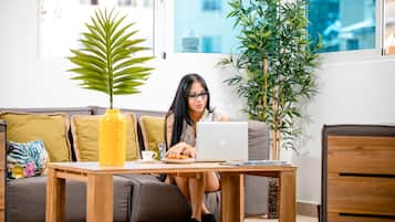 Uma pessoa sentada num sofá com um laptop, uma mesa de madeira com uma planta e uma garrafa amarela à frente.