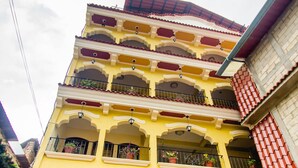 Um edifício de vários andares com área de recepção, varandas com grades e plantas em vasos.