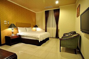 Quarto de hotel com uma cama, duas mesas de cabeceira com luminárias, uma cadeira, uma televisão e uma janela com cortinas.